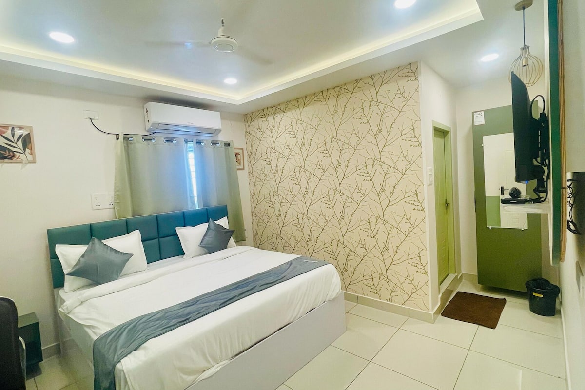 Quarto de hotel com cama, ventoinha no teto, aparelho de ar condicionado, porta verde e espelho.