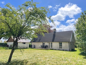 Uma casa de dois andares com varanda coberta, gramado e uma árvore ao primeiro plano.