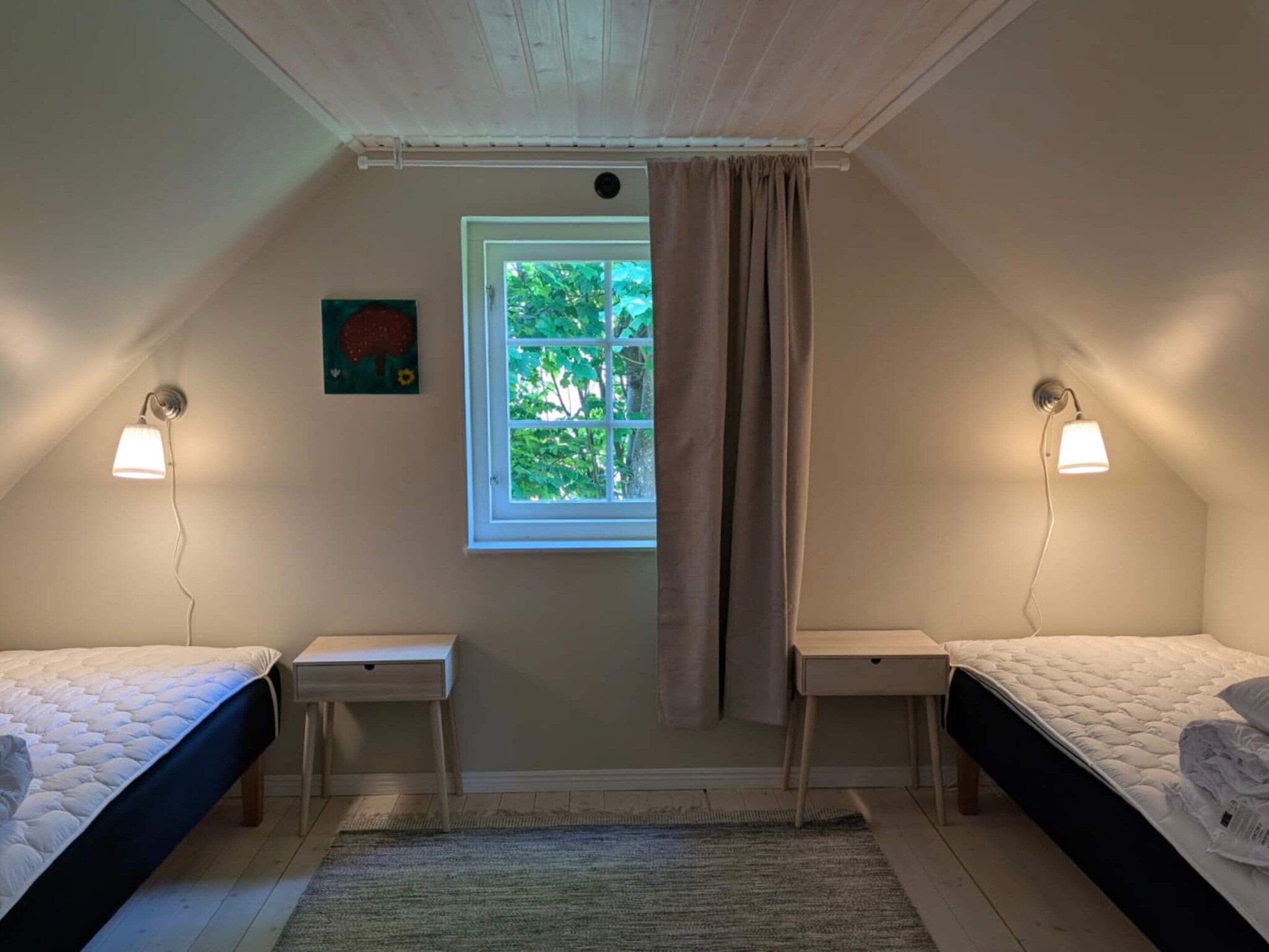Quarto pequeno e acolhedor, com duas camas de solteiro, janela com cortinas e duas luminárias.