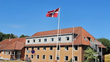 Um edifício com telhado de telhas vermelhas, várias janelas e um mastro com uma bandeira.