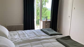 Quarto com cama, janela com cortinas, radiador e porta.