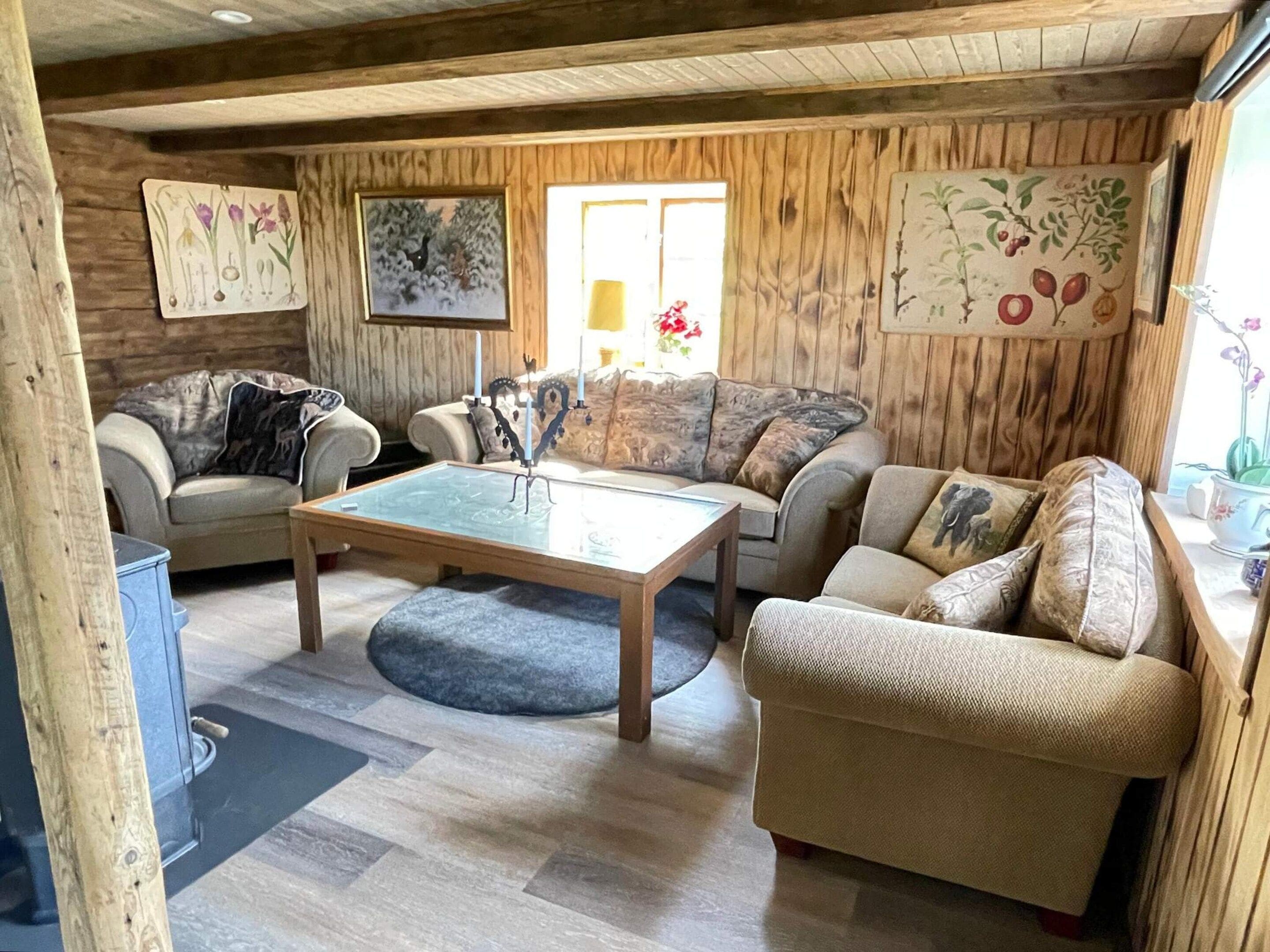 Uma sala de estar acolhedora com paredes de madeira, uma mesa de centro e dois sofás com almofadas estampadas.