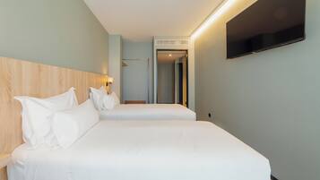 Quarto de hotel com duas camas, uma televisão de tela plana presa na parede e um corredor que leva a outro quarto.