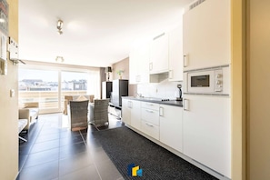 Cozinha moderna com armários brancos, forno embutido e uma grande janela com vista para a cidade.