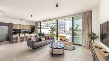 Uma sala de estar moderna com sofá, mesa de centro e cadeiras, cozinha com conjunto de jantar e grandes portas de vidro deslizantes que dão para uma varanda com vista para a piscina.