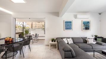 Uma sala de estar moderna com um sofá cinza, uma mesa de jantar com cadeiras e uma pequena mesa lateral com plantas.
