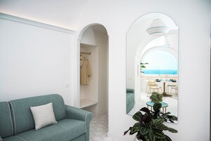 Um interior moderno com um sofá verde-turquesa, uma planta e vista para uma sala de jantar com cadeiras e uma mesa.