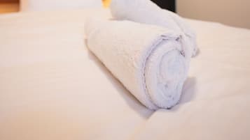 Cama bem arrumada com toalhas brancas dobradas, cabeceira branca e uma porta ao fundo.