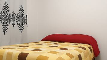 Uma cama com colcha de padrão geométrico, um travesseiro vermelho e uma cortina de renda preta e branca.