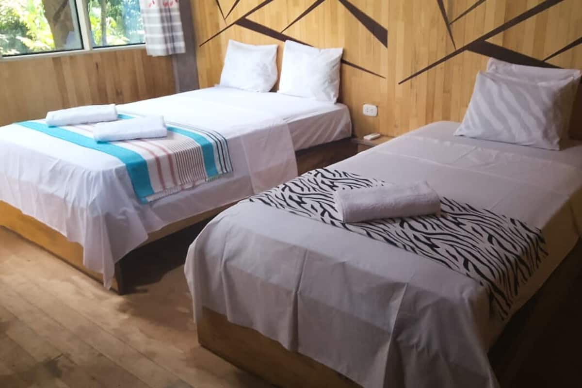 Duas camas de solteiro com roupa de cama branca e mantas com padrão de zebra, cabeceiras de madeira e uma janela com cortinas.