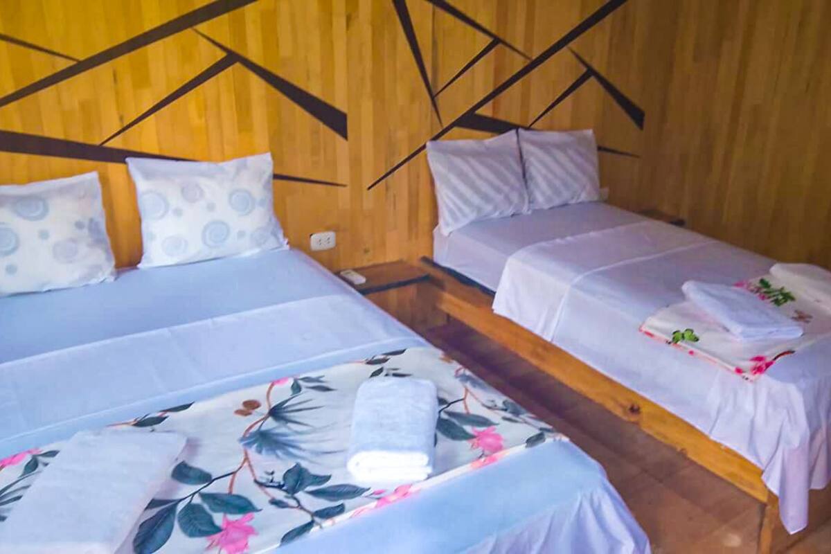 Quarto com duas camas de solteiro, cada uma com cabeceira de madeira e roupa de cama branca.