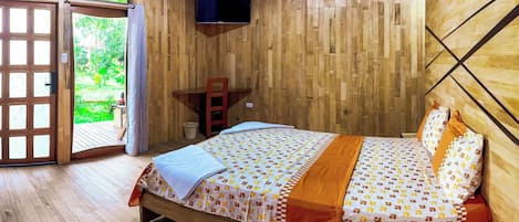 Quarto de madeira com cama, televisão fixada na parede e porta que dá para o exterior.