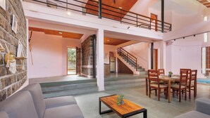 Uma sala de estar ampla com pé direito alto, uma escada que leva a um andar superior e uma área de jantar com móveis de madeira.