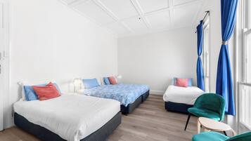 Quarto de hotel com duas camas, uma cadeira, uma mesinha e uma janela com cortinas.