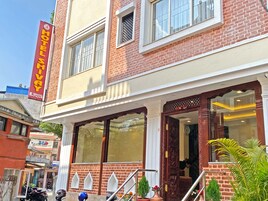 Hotel com placa vermelha, grandes janelas e fachada de tijolos.