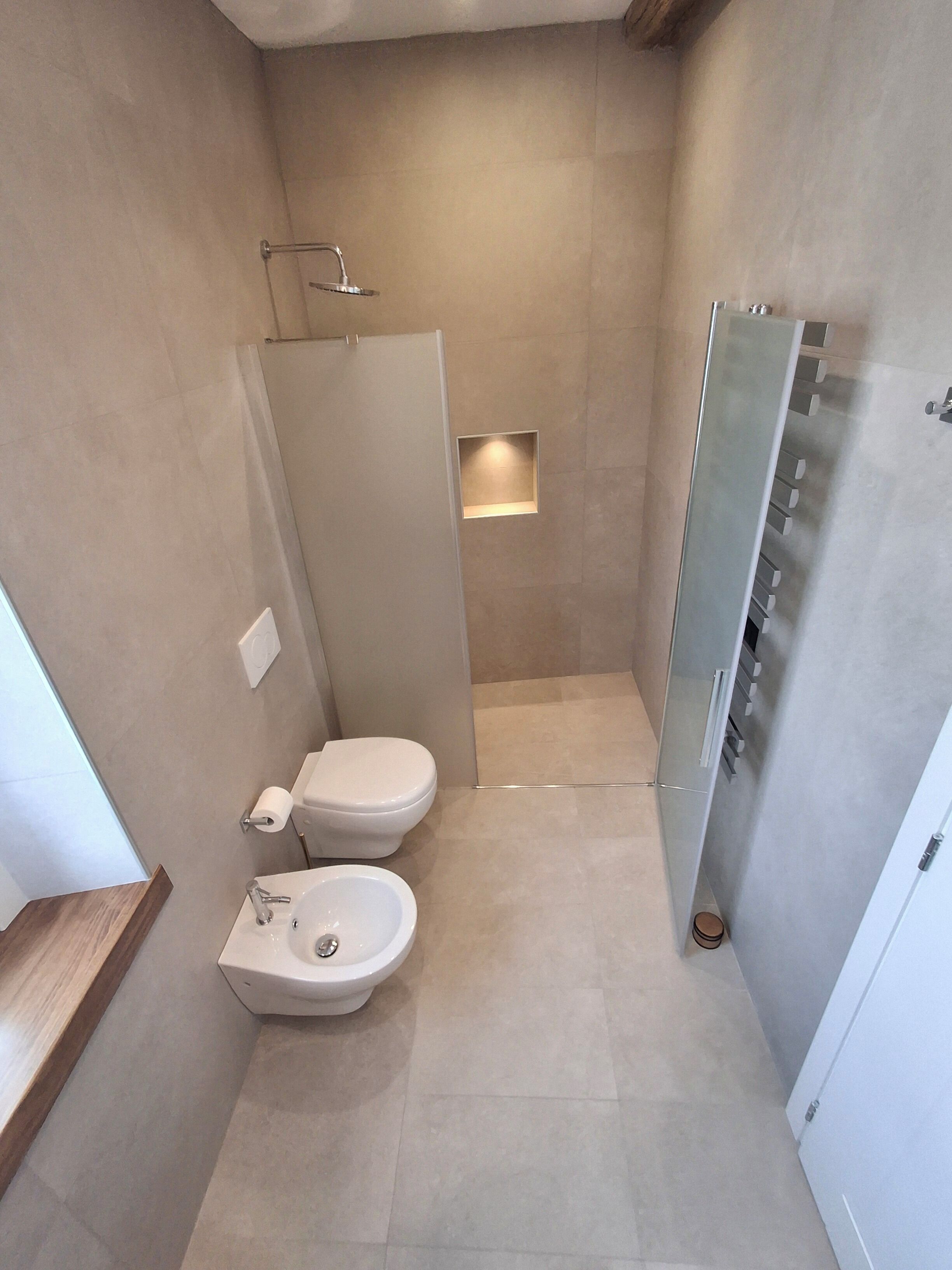 Casa de banho compacta com sanita, bidé e cabine de duche em vidro.