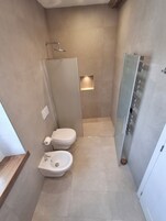 Casa de banho compacta com sanita, bidé e cabine de duche em vidro.