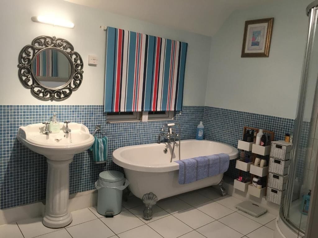Um banheiro com pia assentada em pedestal, banheira independente, toalha listrada, espelho com moldura ornamentada e área de chuveiro revestida em azulejo.