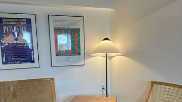 Um quarto acolhedor com duas cadeiras de vime, uma mesa de madeira e um abajur. Cartazes decoram a parede.