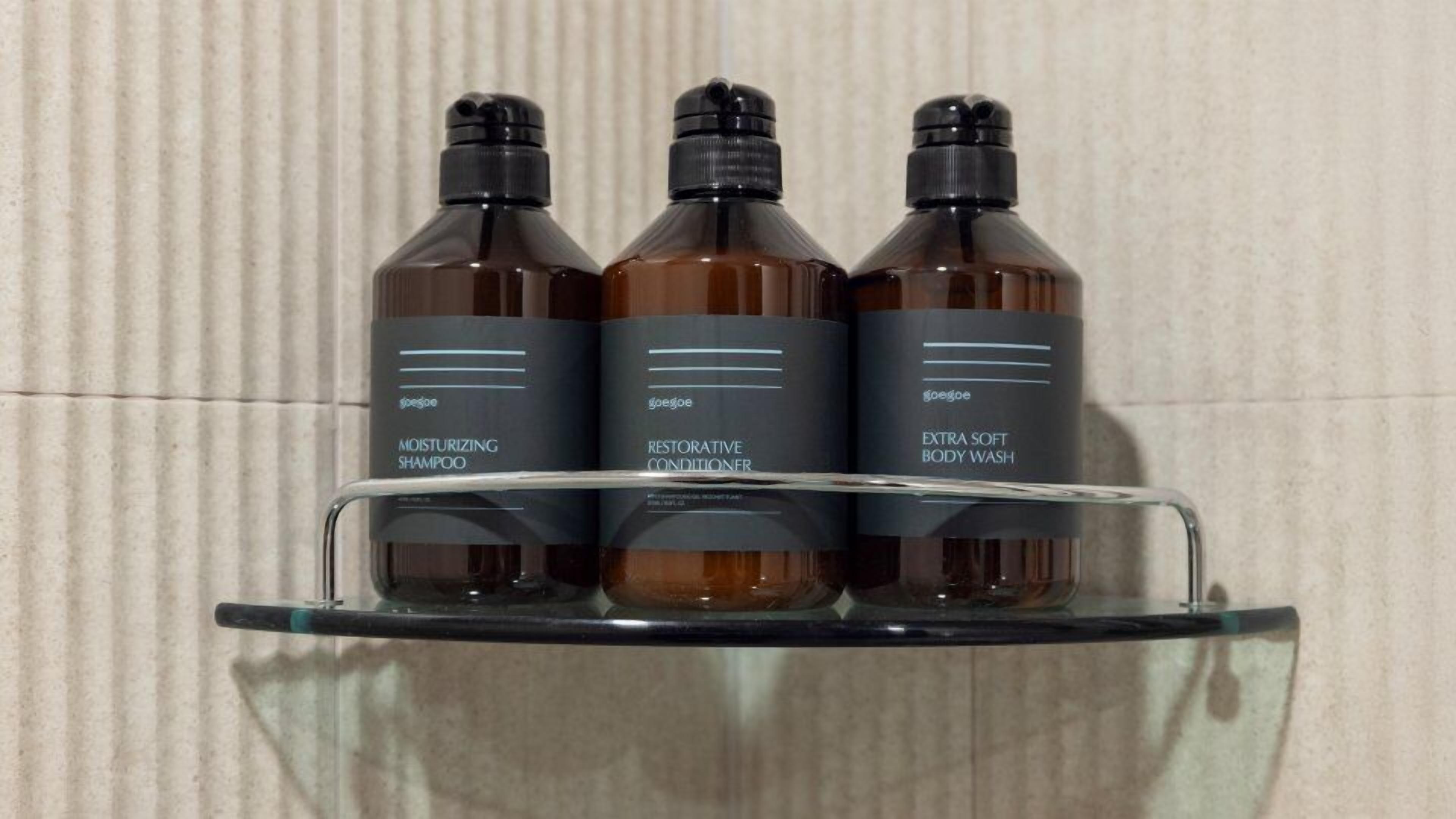 Três frascos de shampoo e condicionador em uma prateleira de vidro.