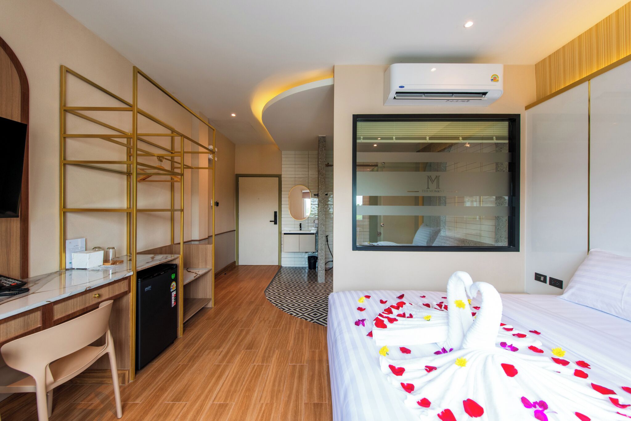 Quarto de hotel com uma cama, escrivaninha, geladeira, televisão e aparelho de ar condicionado.