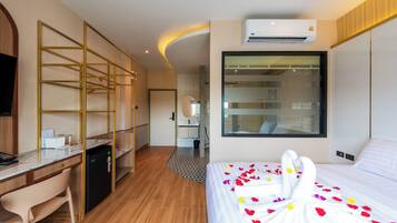 Quarto de hotel com uma cama, escrivaninha, geladeira, televisão e aparelho de ar condicionado.
