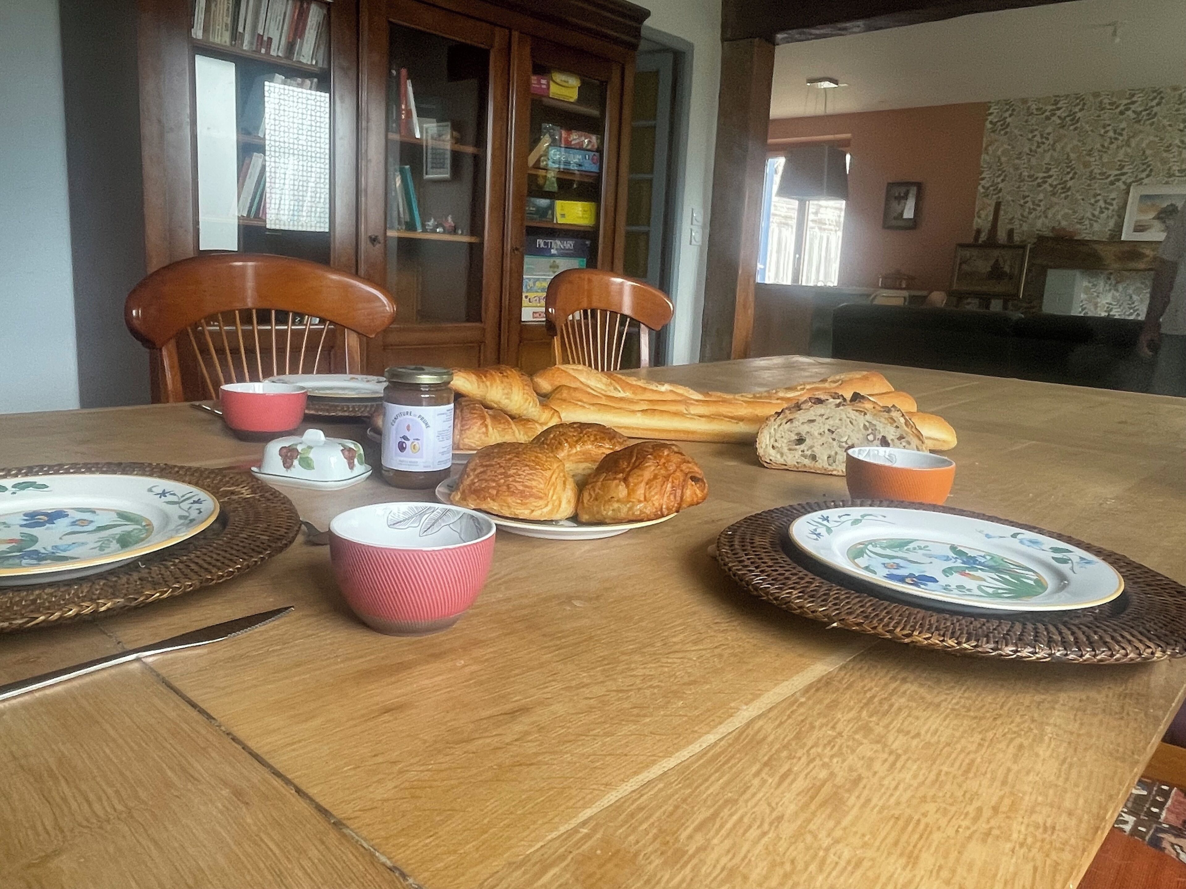 Uma mesa de jantar com pão, pastelaria e chávenas de chá.