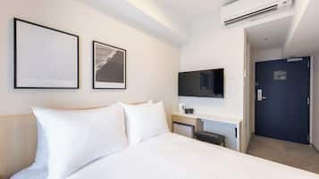 Quarto de hotel com uma cama, duas imagens emolduradas, uma televisão de ecrã plano, uma máquina de café e uma porta.