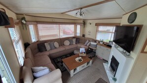 Interior aconchegante de uma motorhome, com sofá seccional, mesa de centro, televisão e pequena cozinha.