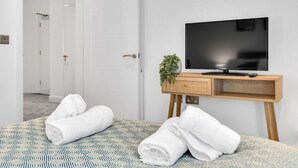 Quarto de hotel com uma cama, uma TV sobre um suporte de madeira e uma porta que dá para outro cômodo.