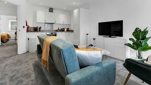 Uma sala de estar moderna com um sofá, uma televisão e uma cozinha ao fundo.