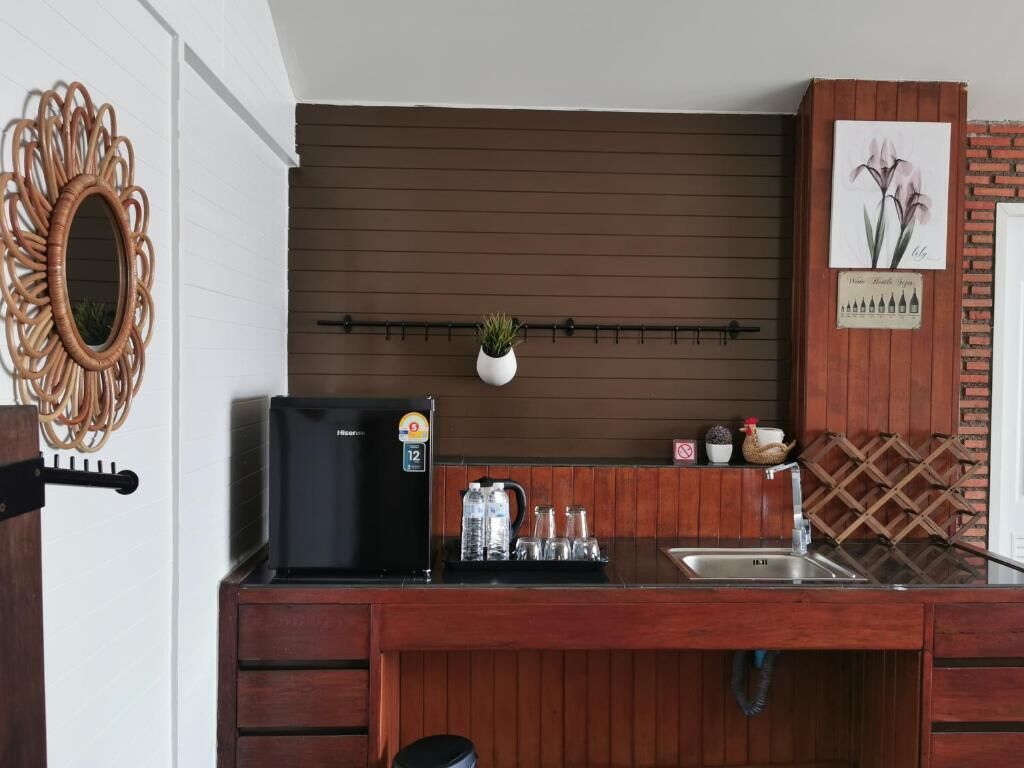 Cozinha compacta com geladeira preta, cafeteira e planta pendente.