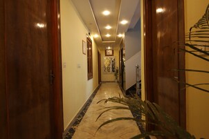 Um corredor com portas de madeira, piso de mármore e iluminação embutida no teto.