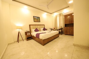 Quarto de hotel com cama, escrivaninha, cadeira, luminária e ventilador de teto.
