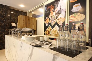 Um buffet de café da manhã com diversos alimentos, garrafas de vidro transparente e um armário de madeira.