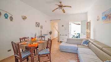 Uma sala de jantar com uma mesa posta para quatro pessoas, um sofá e um ventilador de teto.