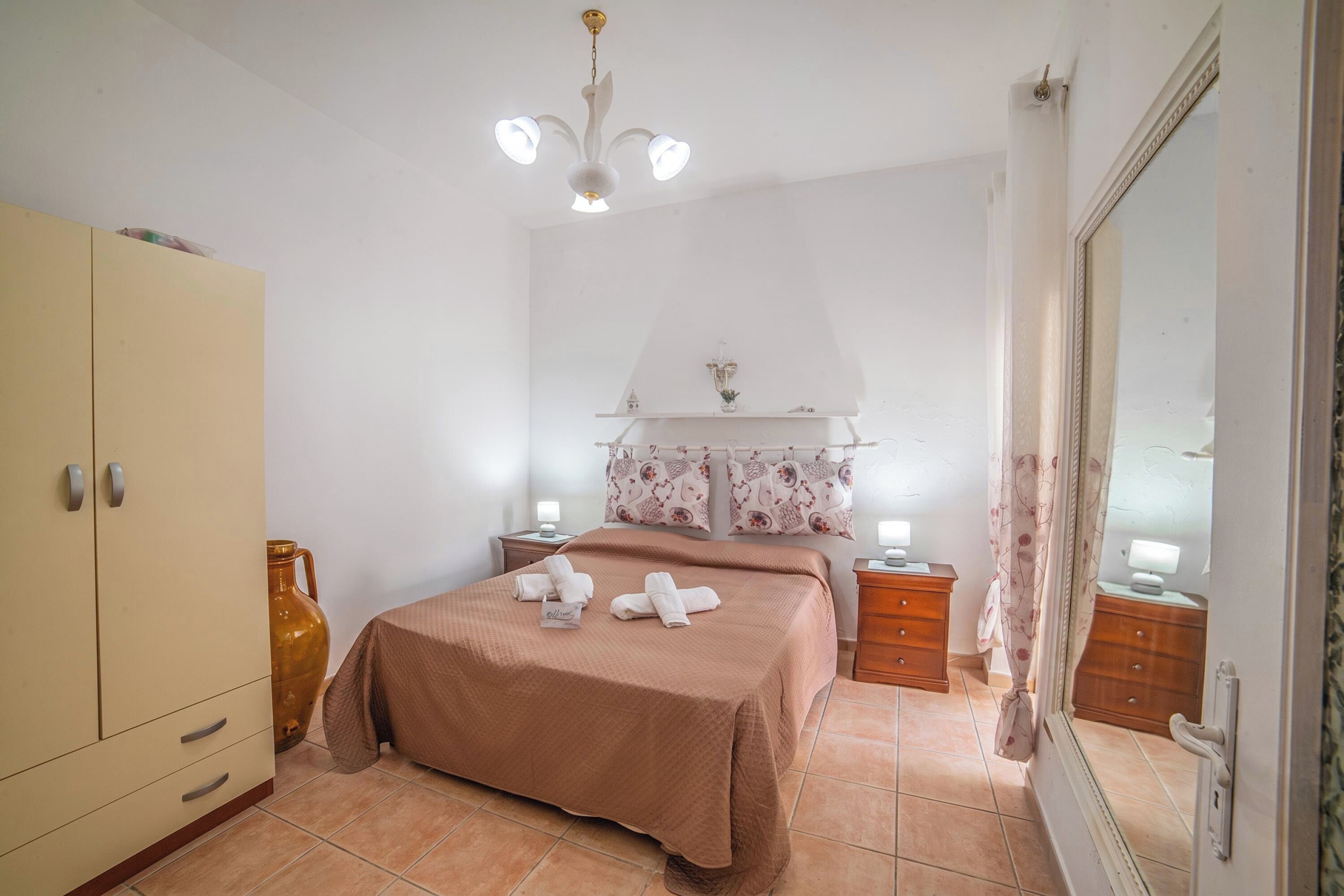 Quarto com cama, mesas de cabeceira, guarda-roupa e espelho.