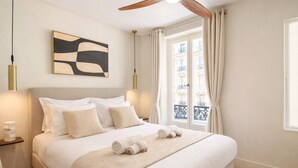 Quarto de hotel com uma cama grande, um ventilador de teto, uma janela com cortinas e um quadro na parede.