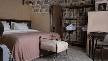 Quarto com parede de pedra, cama com cabeceira, mesa de cabeceira, uma cadeira e guarda-roupa.