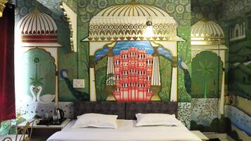 Quarto de hotel com uma cama, uma escrivaninha e um mural de um edifício e pavões.