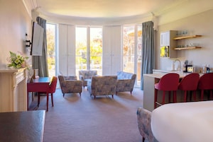Quarto de hotel com uma cama grande, área de refeições com cadeiras, uma mesinha, sofá, lareira e vista para o exterior.