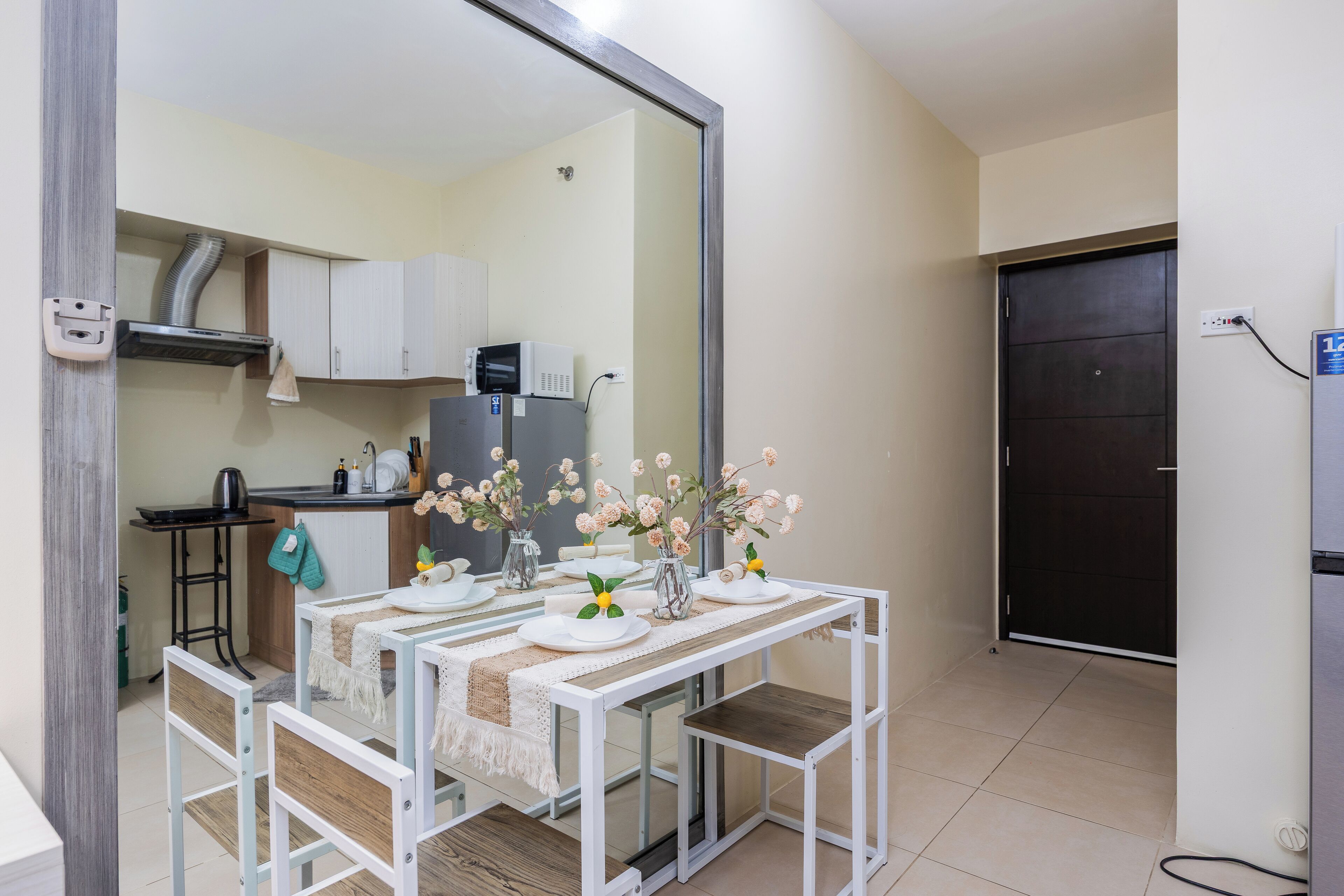 Uma sala de jantar com uma mesa posta para dois, uma cozinha ao fundo e uma porta à direita.