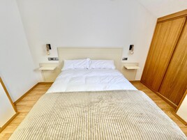 Cama bem arrumada com lençóis brancos em quarto com piso de madeira e guarda-roupa de madeira.