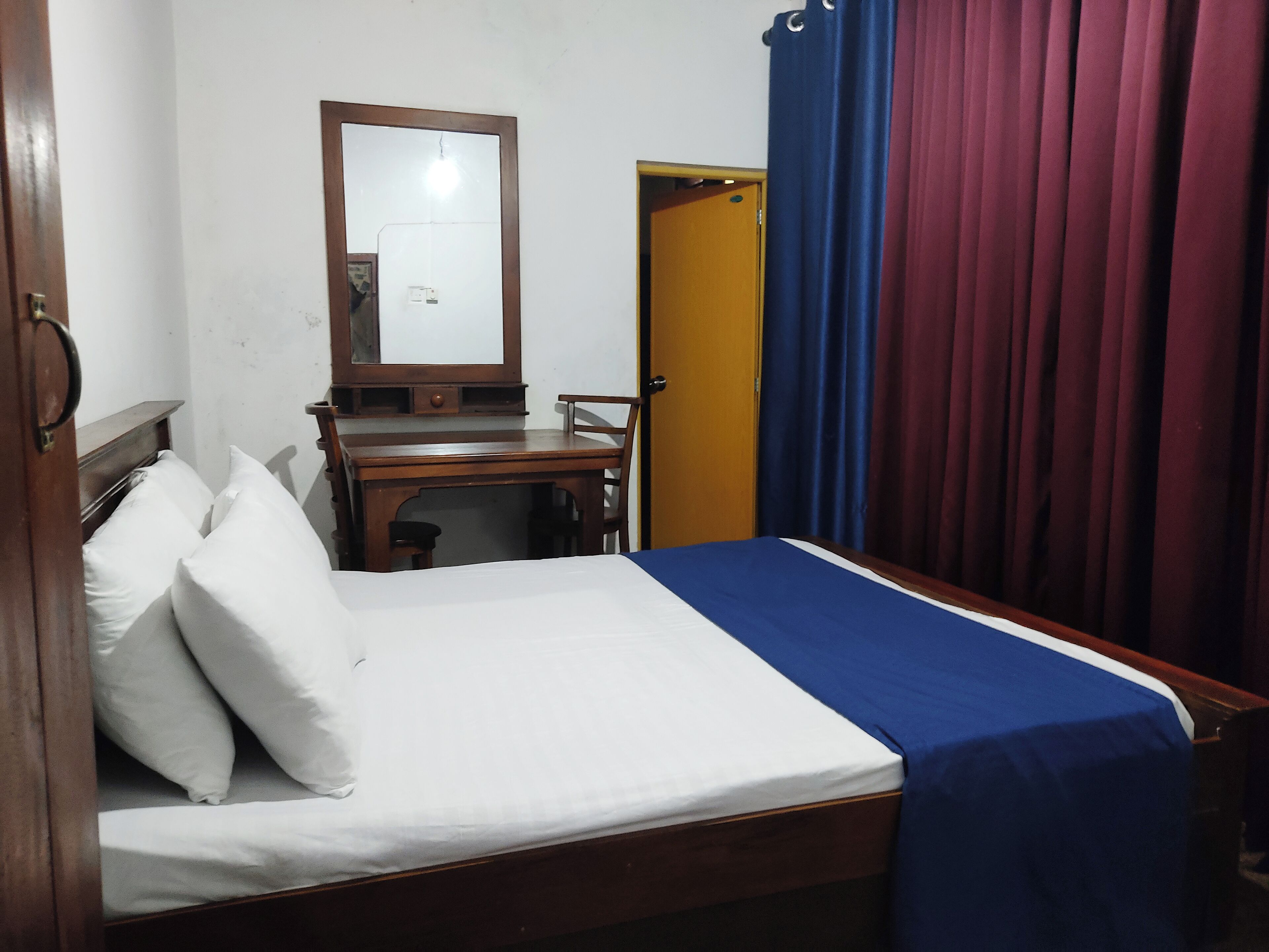 Quarto com cama de madeira, escrivaninha, cadeira, espelho e porta.