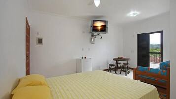 Quarto com uma cama, televisão na parede, mesa pequena com cadeiras e janela com persianas.