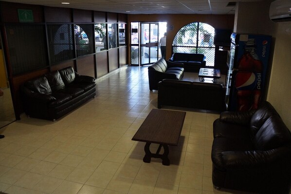 Um lobby com sofás de couro, uma mesa de centro de madeira e uma máquina de vendas.