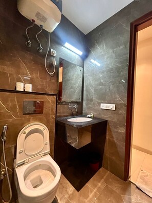 Casa de banho com sanita, lavatório e espelho. Tem um secador de cabelo na parede e um chuveiro.