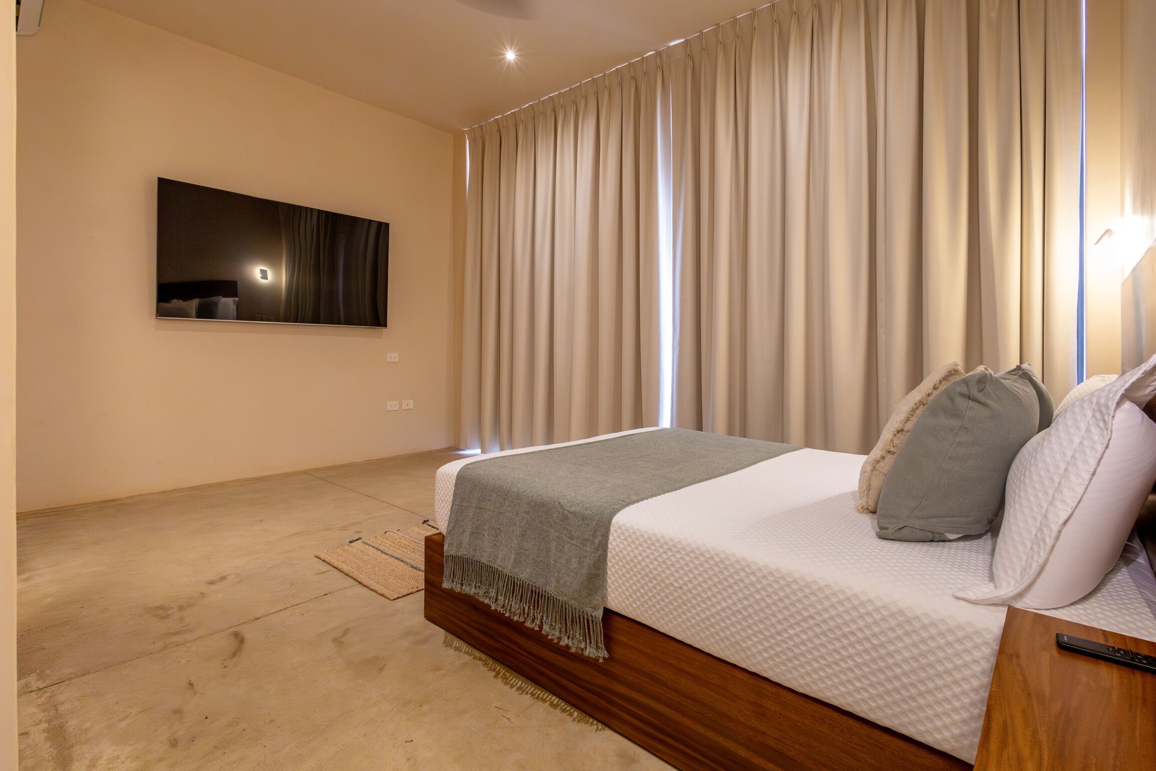Quarto moderno com uma cama grande, televisão de tela plana na parede e uma janela ampla com cortinas.