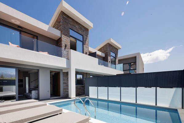 Uma casa moderna de dois andares, com piscina, janelas amplas e uma varanda.
