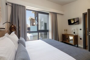 Quarto de hotel com uma cama grande, televisão presa à parede, porta de vidro deslizante para a varanda e mesa consola de madeira.